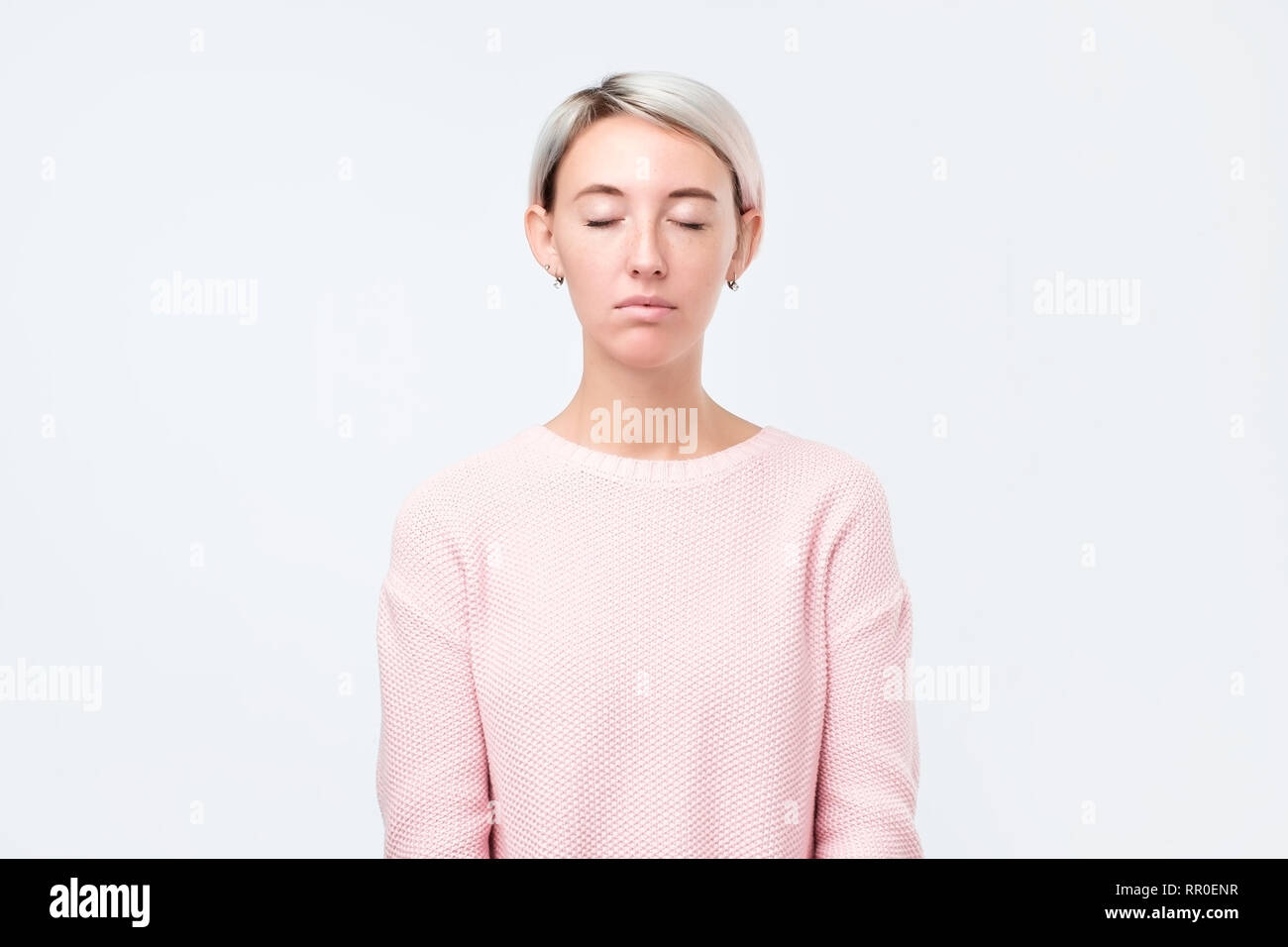 Young european woman in pink sweater closing eyes. No emotion on her ...