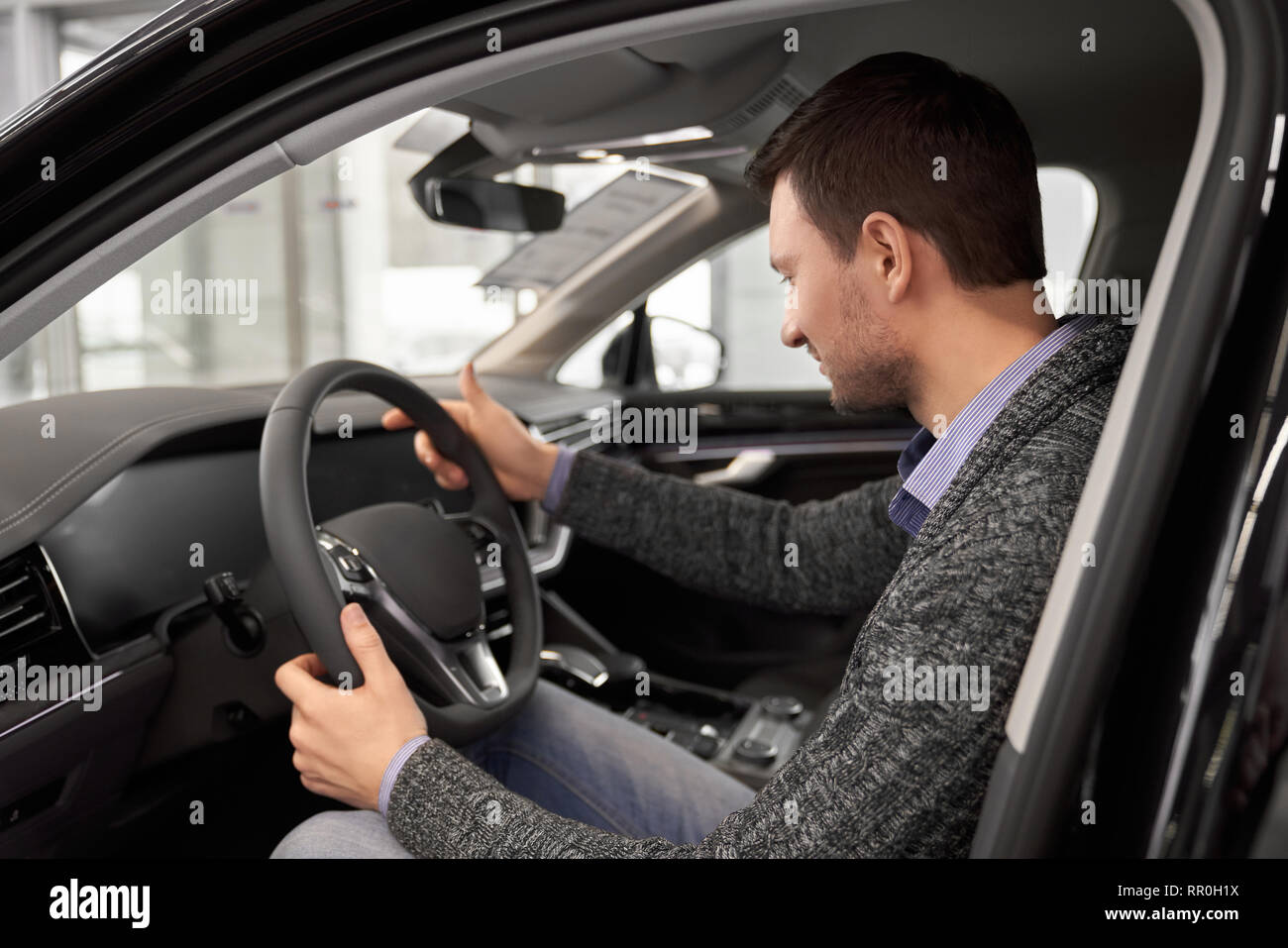 Happy male customer of car center sitting in driver's seat of car cabin ...