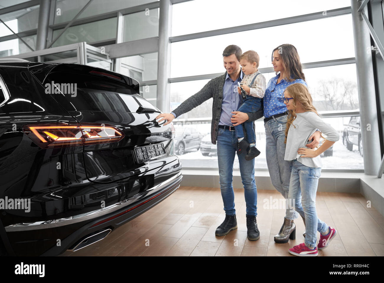 Cheerful parents showing to children new car in car dealership. Happy ...