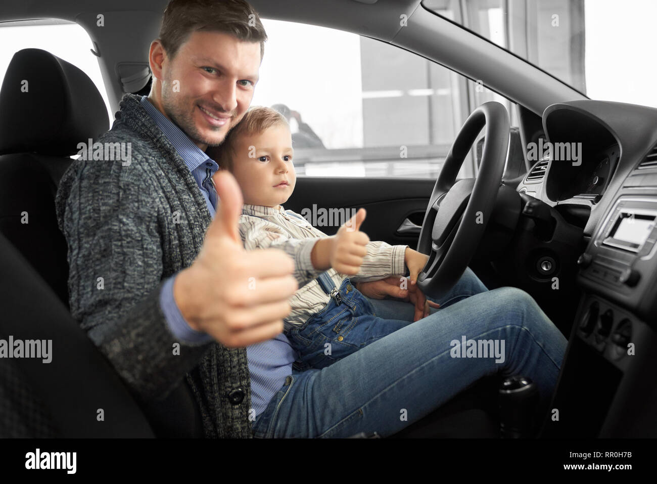 Father and son sitting in driver's seat of new expensive car, showing ...
