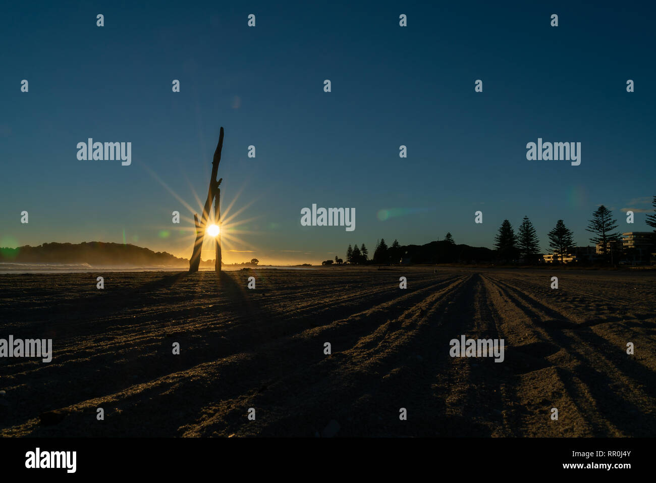Tracks from beach grooming leading away towards sunrise with sun burst ...