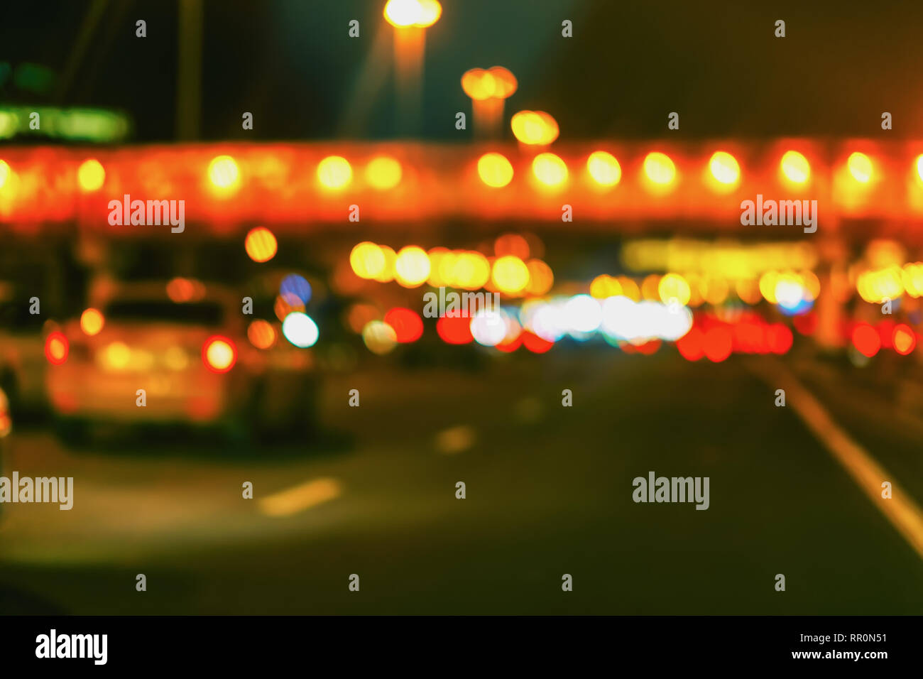Blurred overhead lighted pedestrian bridge at night, moving cars, bokeh ...