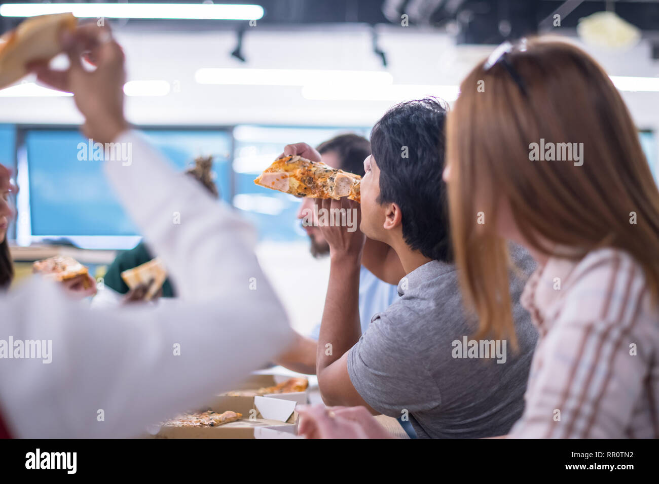 Friendly diverse multiethnic business team eating sharing pizza together in startup office ...
