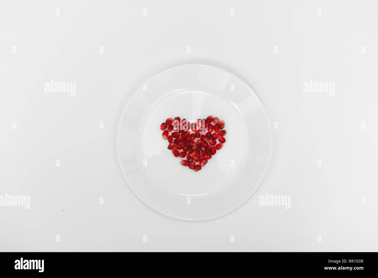 On a white plate from pomegranate seeds composite heart shape. White ...