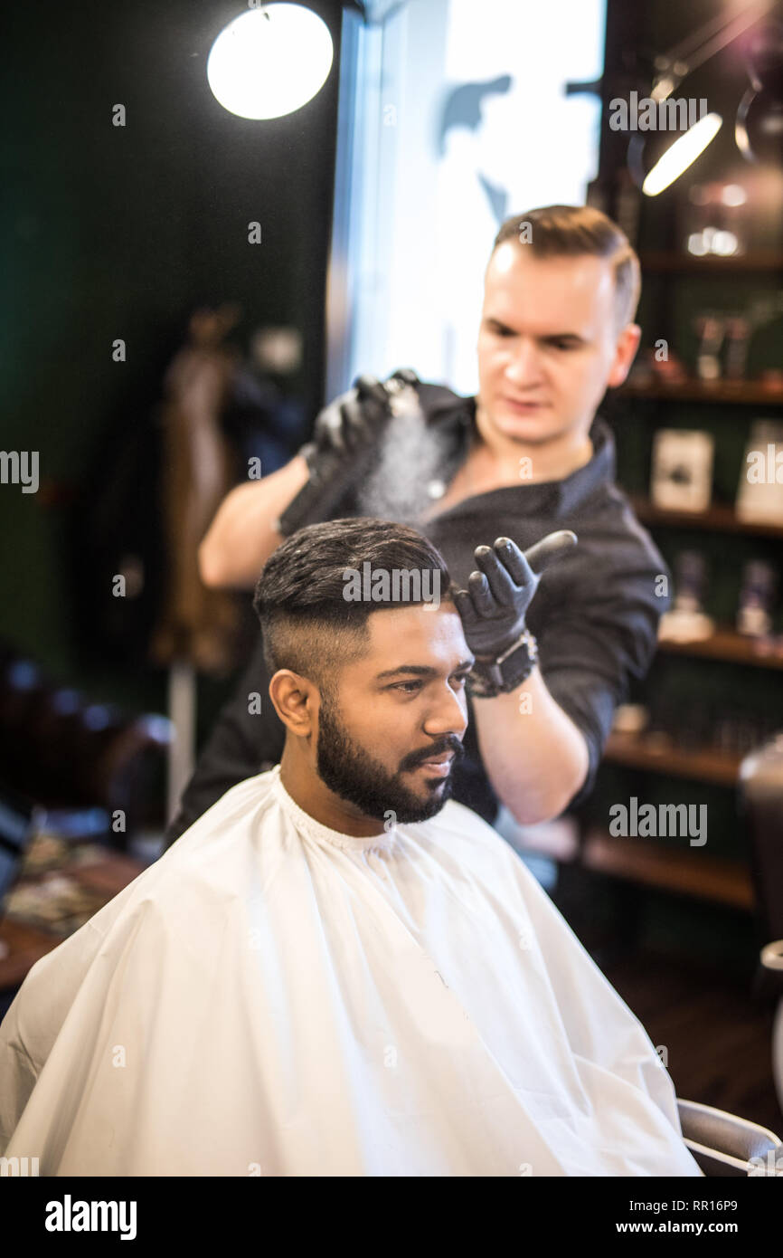 Barber combs his hair to young guy with a beard and mustache and ...