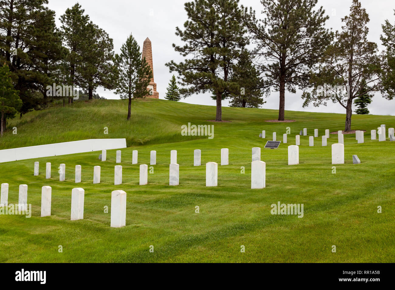 A large obelisk monument sits atop a hillside over the white headstone ...