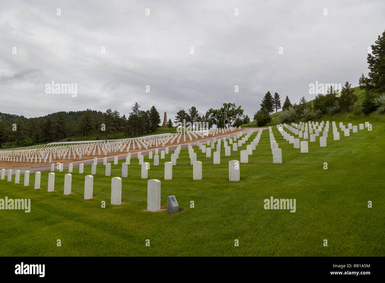 A large obelisk monument sits atop a hillside over the white headstone ...