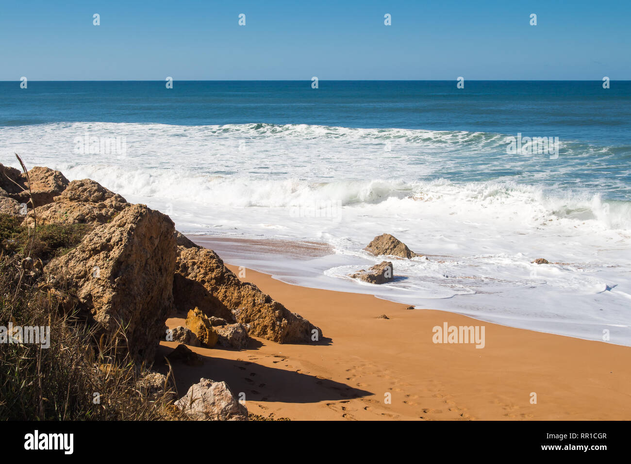 Rocks on the clean beach with dark yellow sand. Foamy waves of the ...