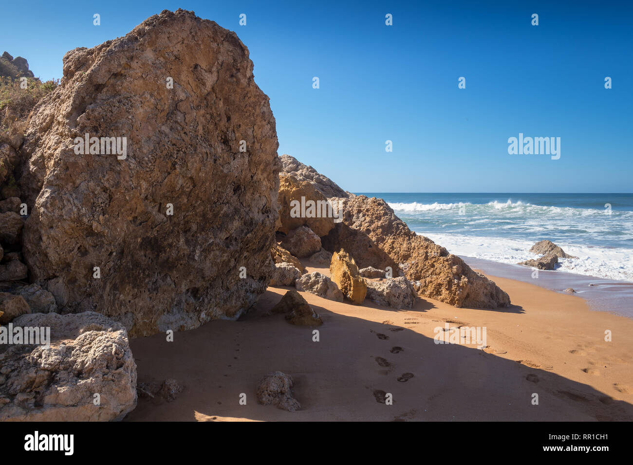 Rocks on the clean beach with dark yellow sand. Foamy waves of the ...