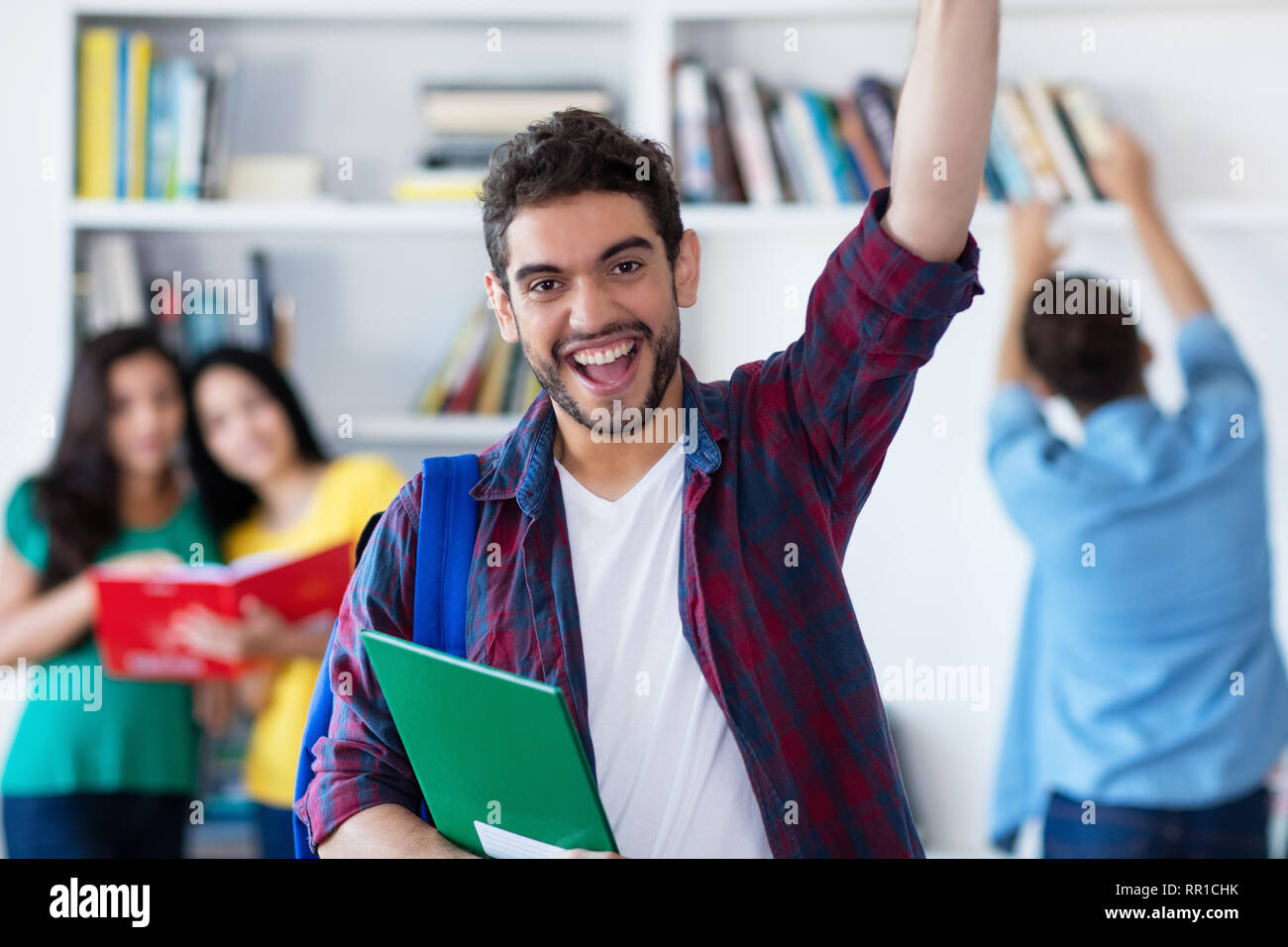 Cheering spanish male student with group of students at library of ...