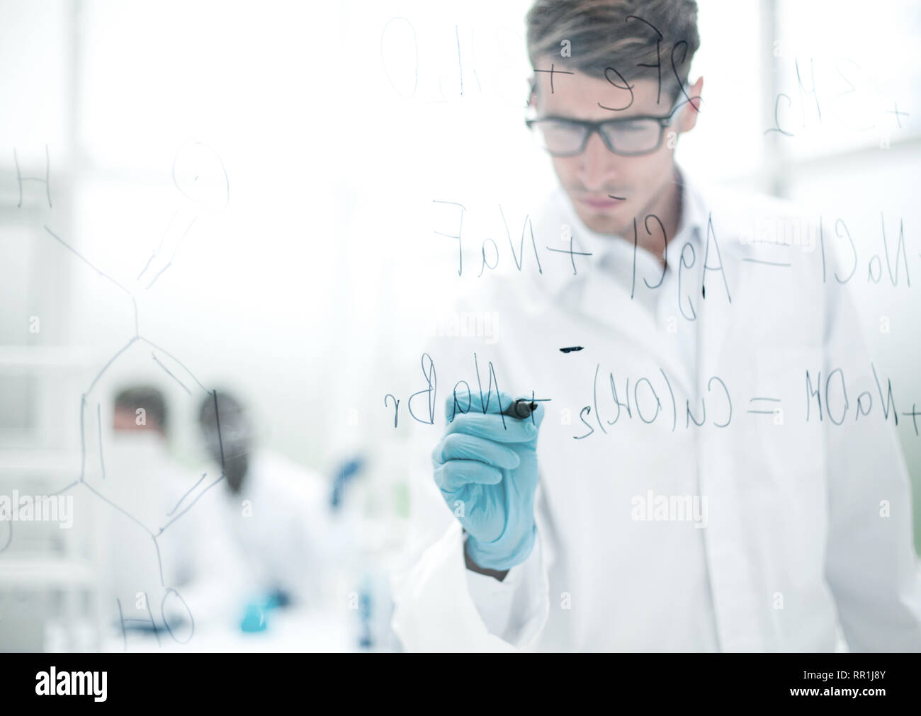 serious scientist writes a chemical formula on a glass Board Stock ...