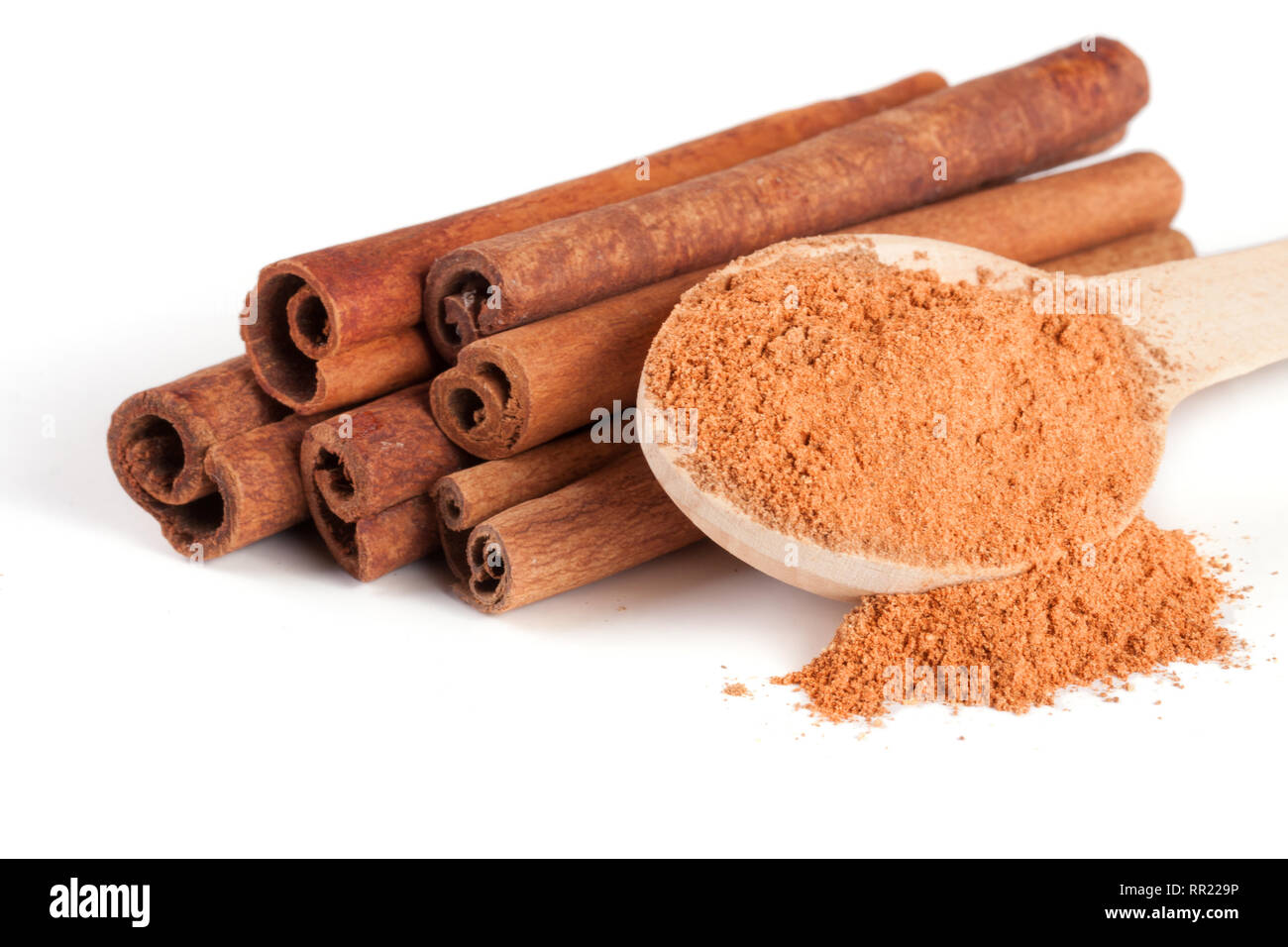 a stack of cinnamon sticks and powder with spoon isolated on white ...
