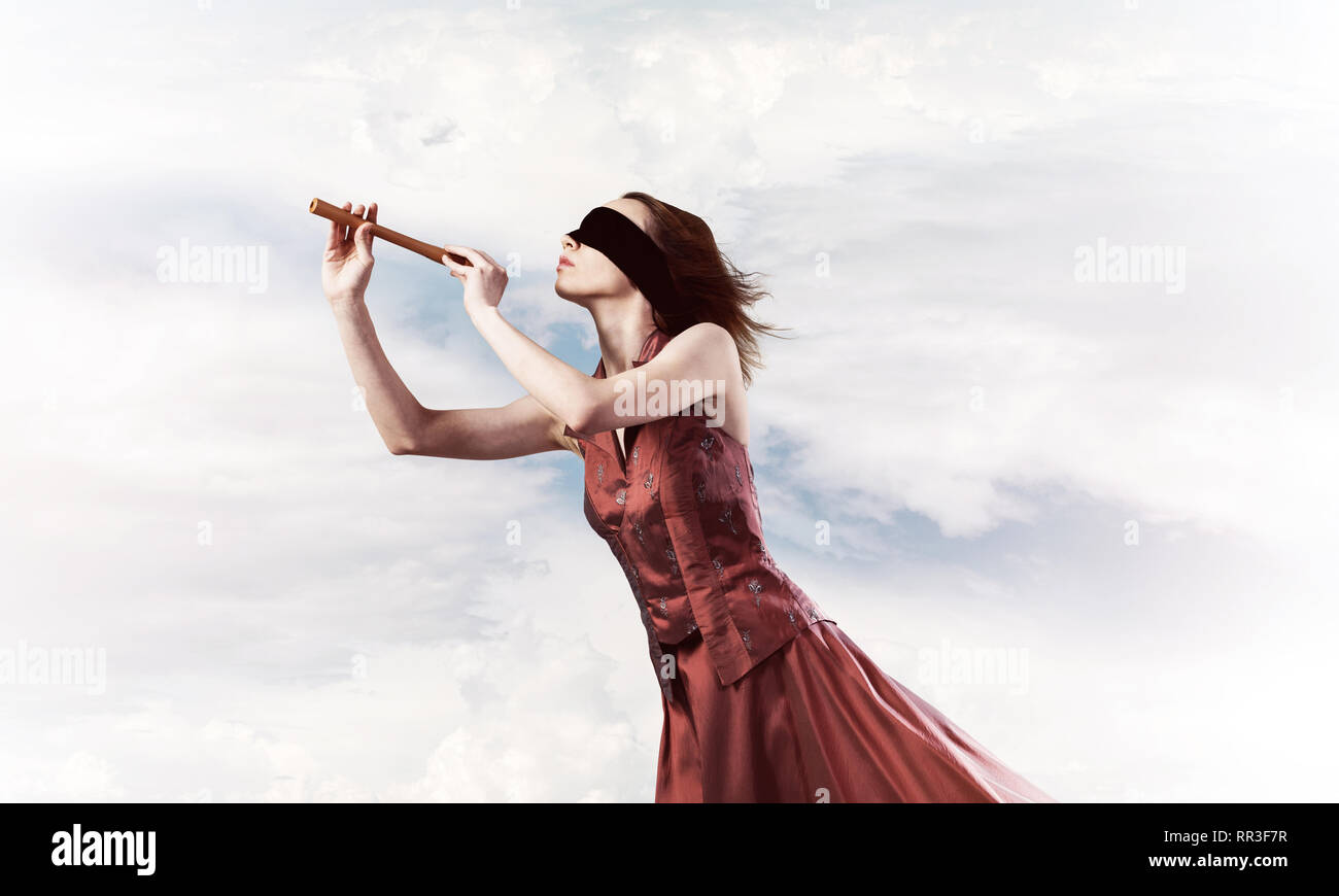 Young pretty woman in red long gress playing fife on cloudy background ...