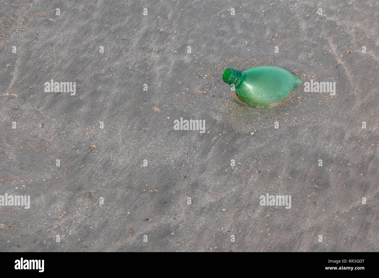 Empty plastic soft drink bottle embedded in silty beach sand. For ...