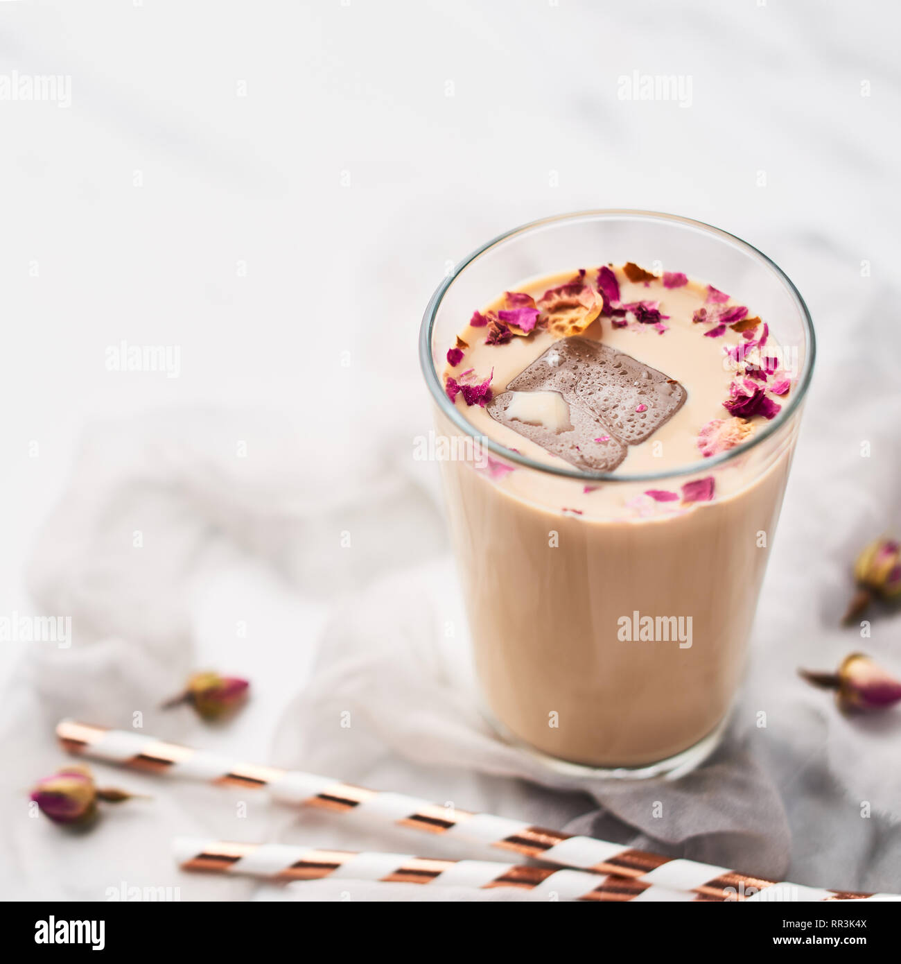 Iced coffee with rose and cardamom in a tall glass surrounded by dried ...