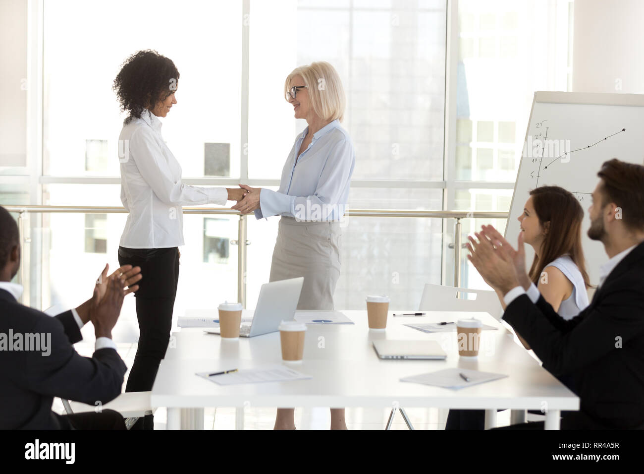 Aged female boss shaking hands with promoted worker Stock Photo - Alamy