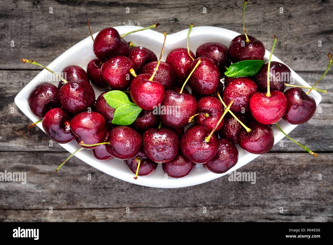 Fresh red cherries on a white plate in shape of lips, on wooden ...