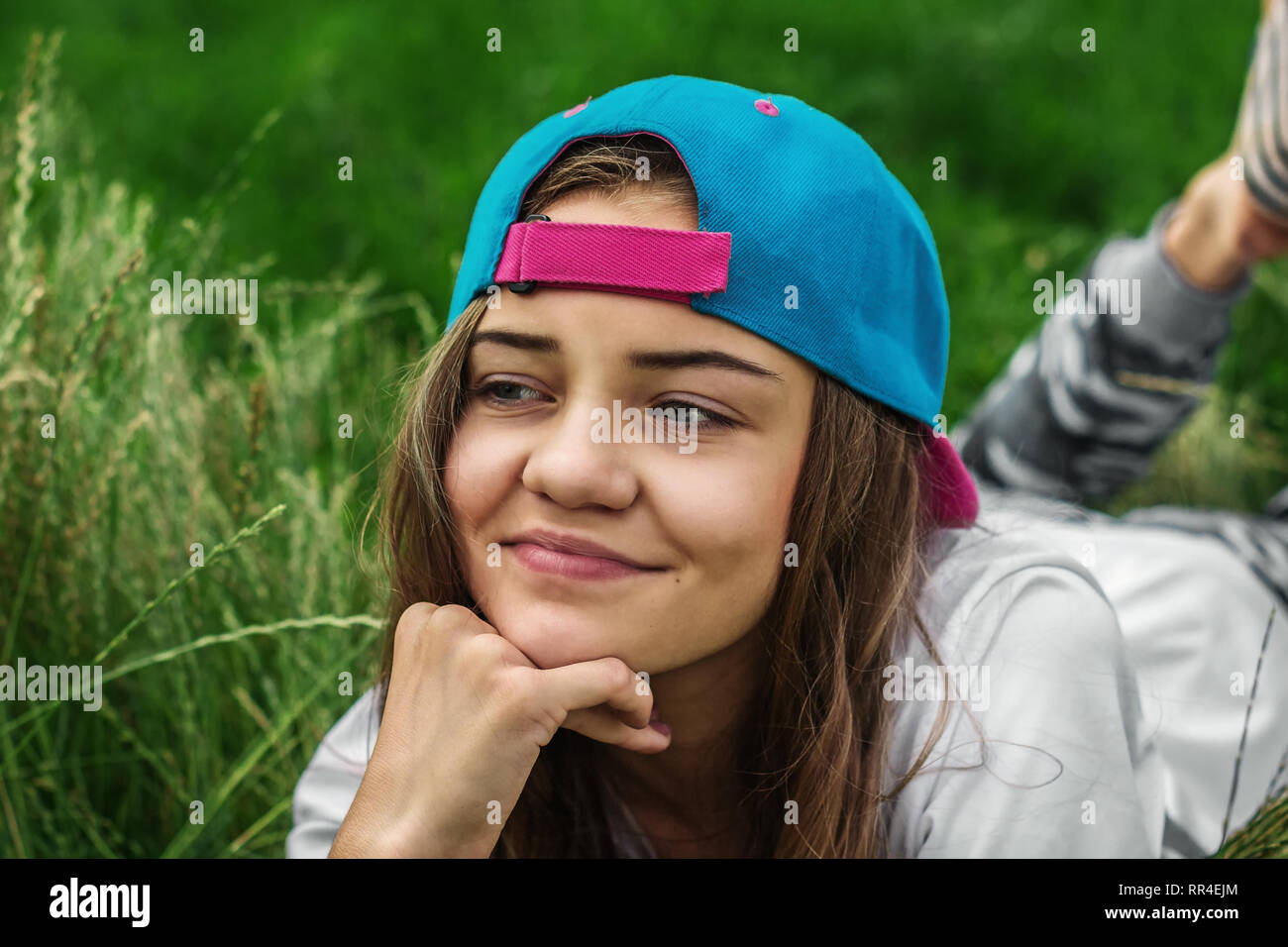 Beautiful white Caucasian girl in a baseball cap lies on a green grass ...