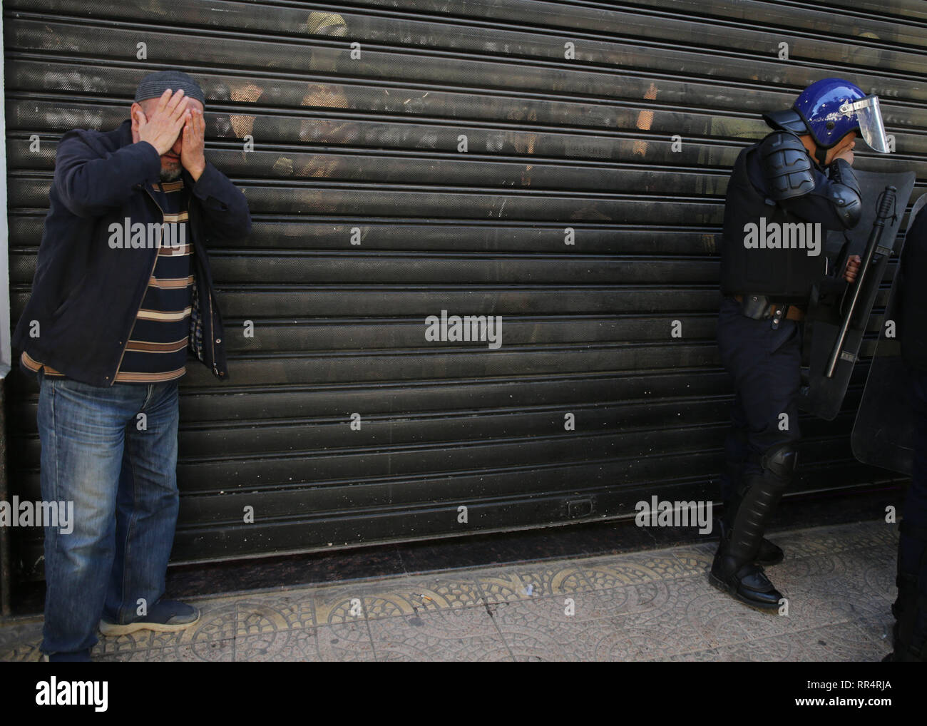 Algiers, Algeria. 24th Feb, 2019. A protester and a policeman cover ...