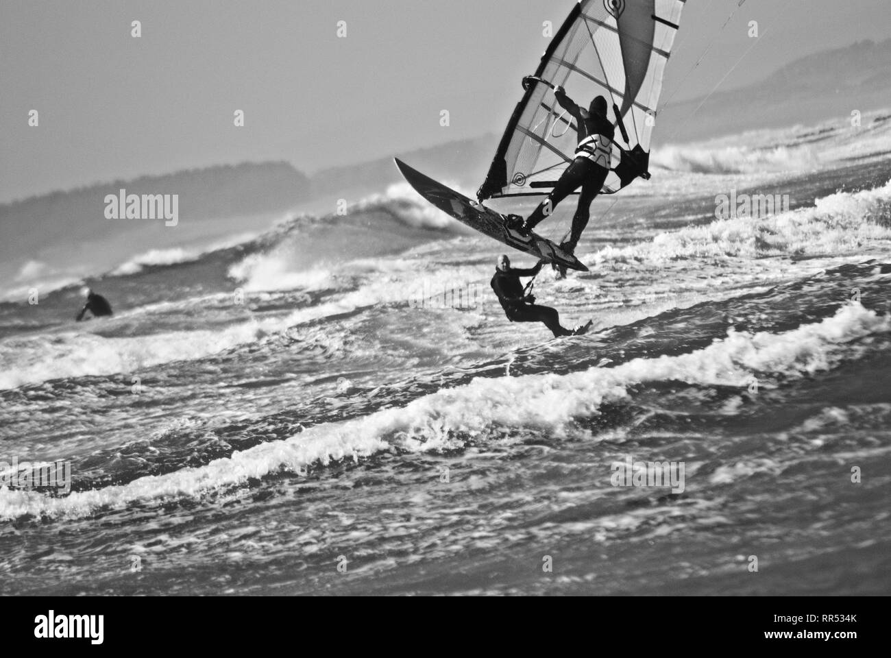 A wind surfer becomes airborne on dramatic white water in grey overcast ...