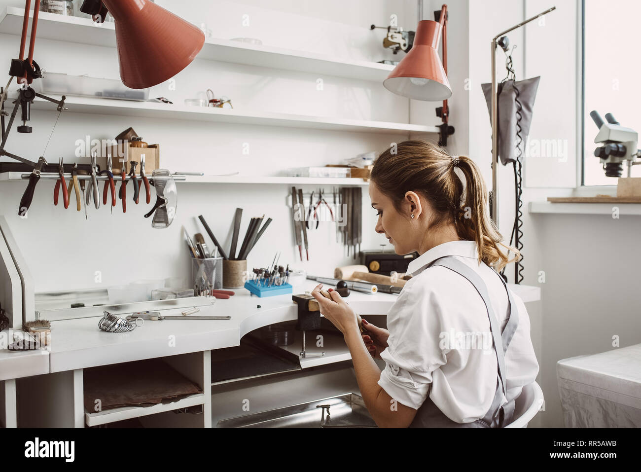 Routine work. Back view of young female jeweler sitting at her jewelry ...