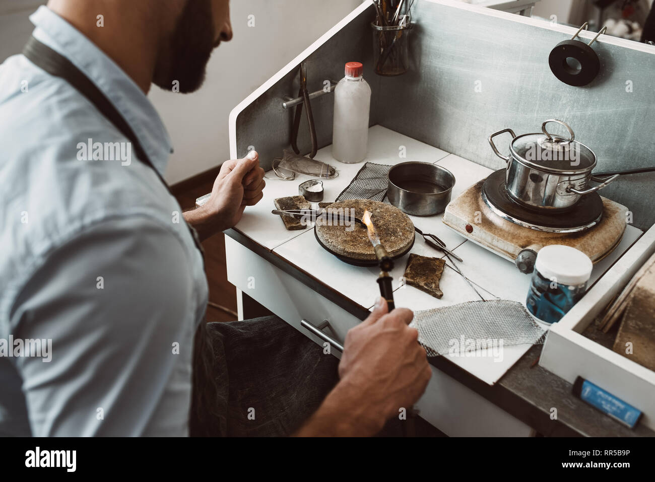 Working with a fire. Side view of young male jeweler ready to solder a ...