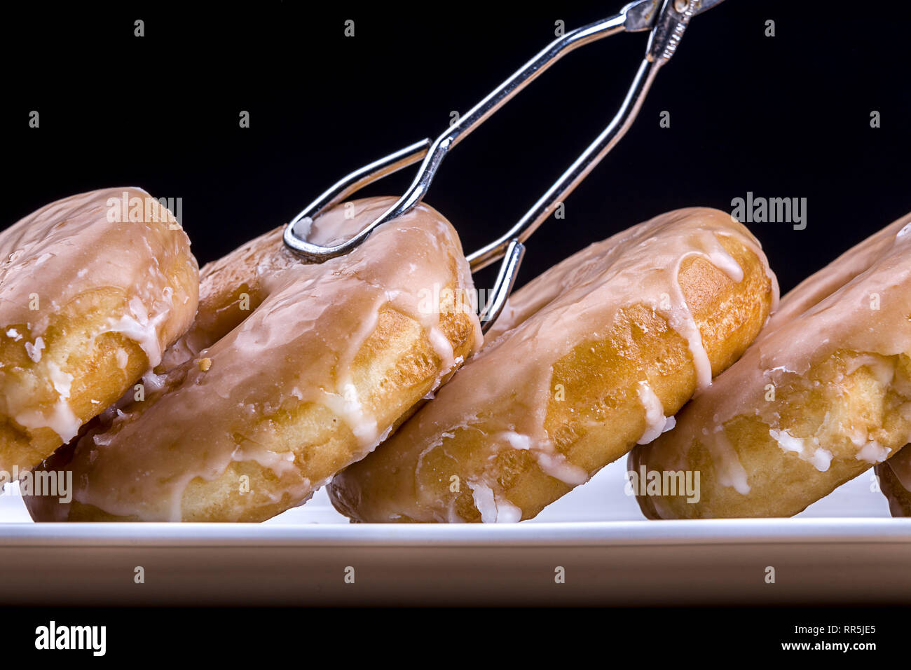 A macro photo of tongs reaching for fresh glazed doughnuts Stock Photo ...