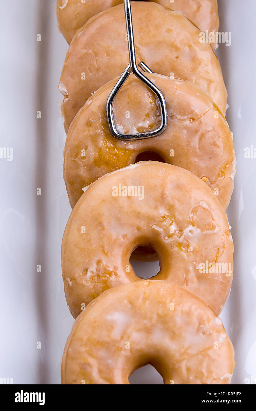 A macro photo of tongs reaching for fresh glazed doughnuts Stock Photo ...