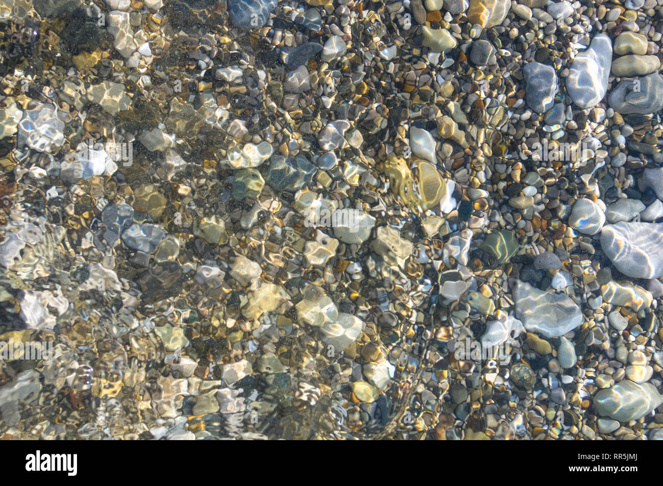 sea pebble beach with multicoloured stones, transparent waves with foam ...