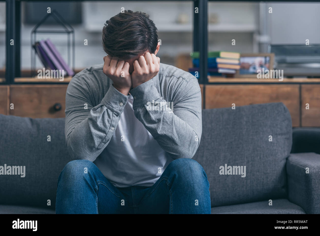 man sitting on couch, crying and and covering face with hands at home ...