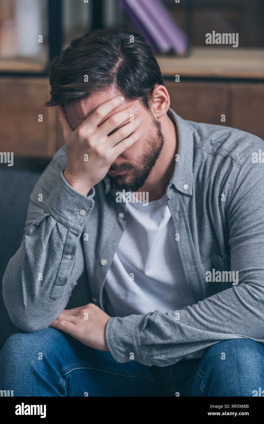 upset man sitting, crying and covering face with hand at home Stock ...