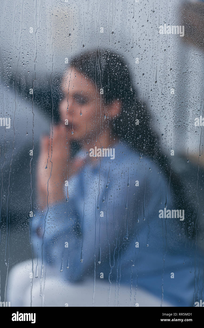 selective focus of raindrops on windows with sad woman sitting and ...