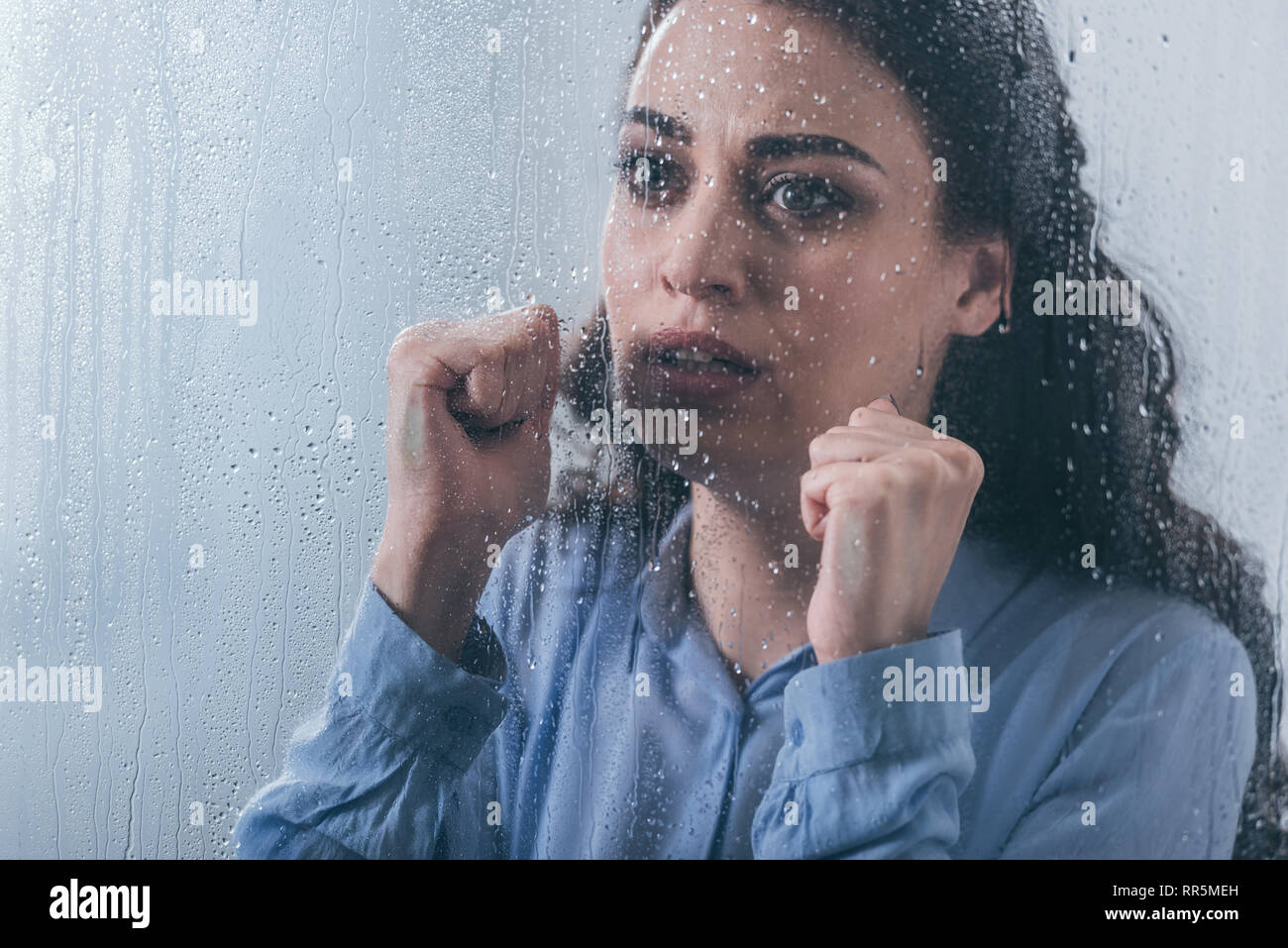 beautiful sad woman with clenched fists looking through window with ...