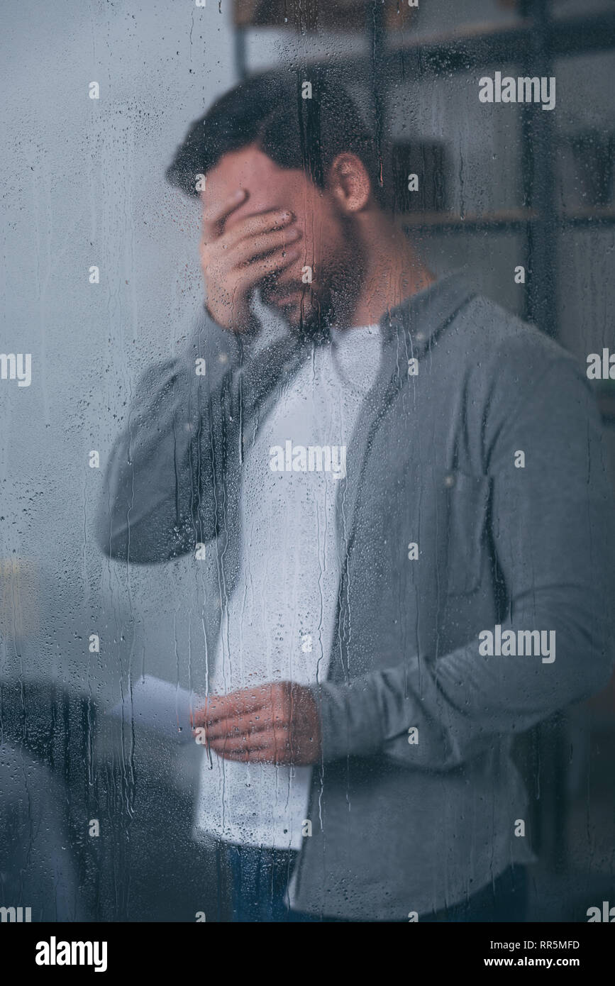 depressed man covering face with hand, holding photograph and crying ...