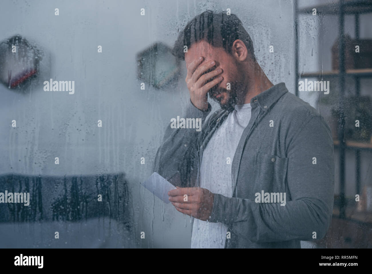 depressed man covering face with hand, holding photograph and crying ...