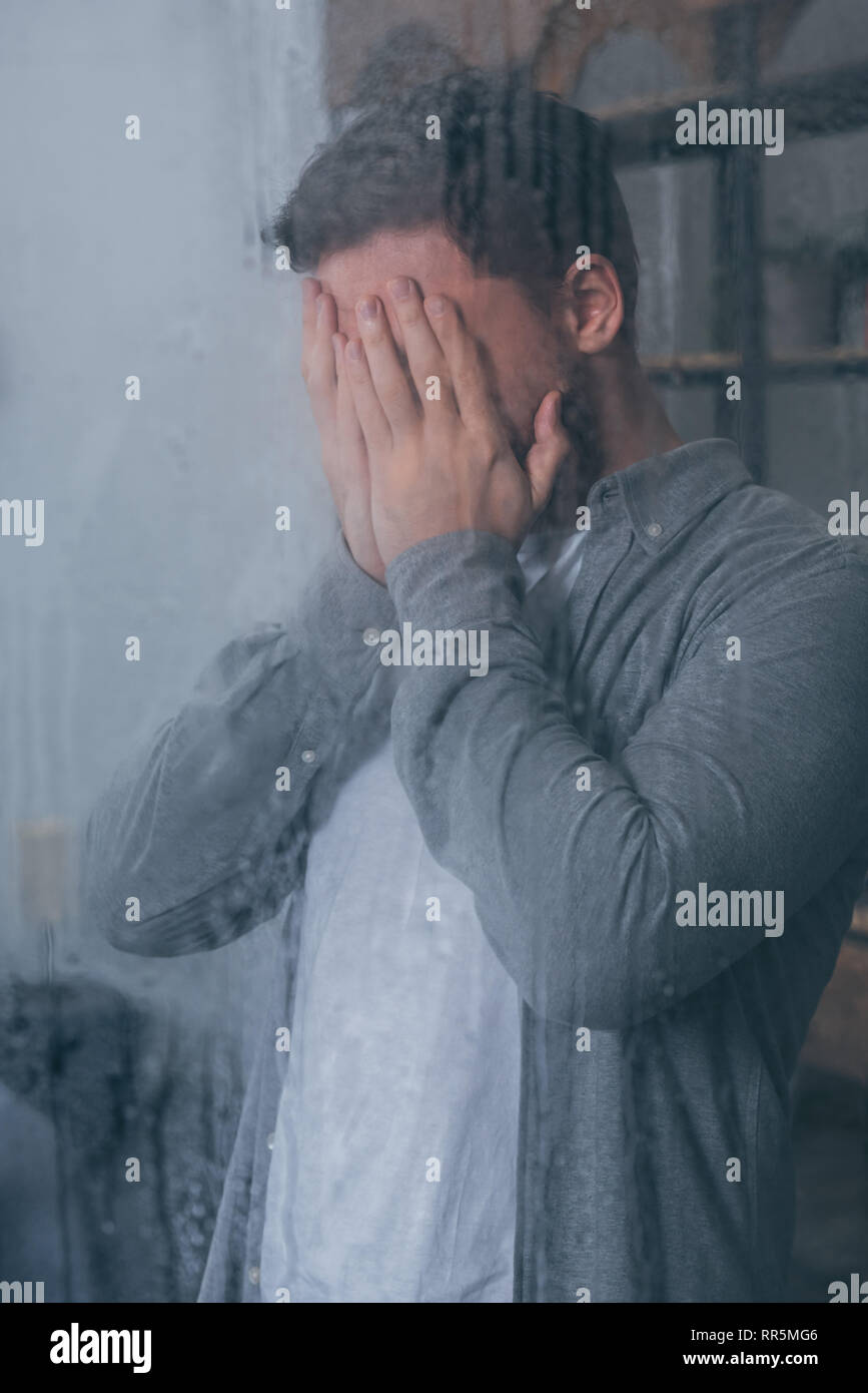 adult man covering face with hands and crying through window with ...