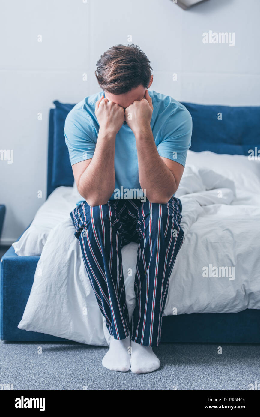 grieving man sitting on bed, covering face with hands and crying at ...