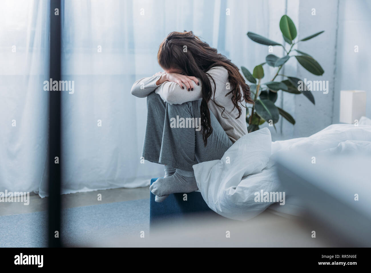 grieving woman sitting, covering face with hands and crying in bedroom ...