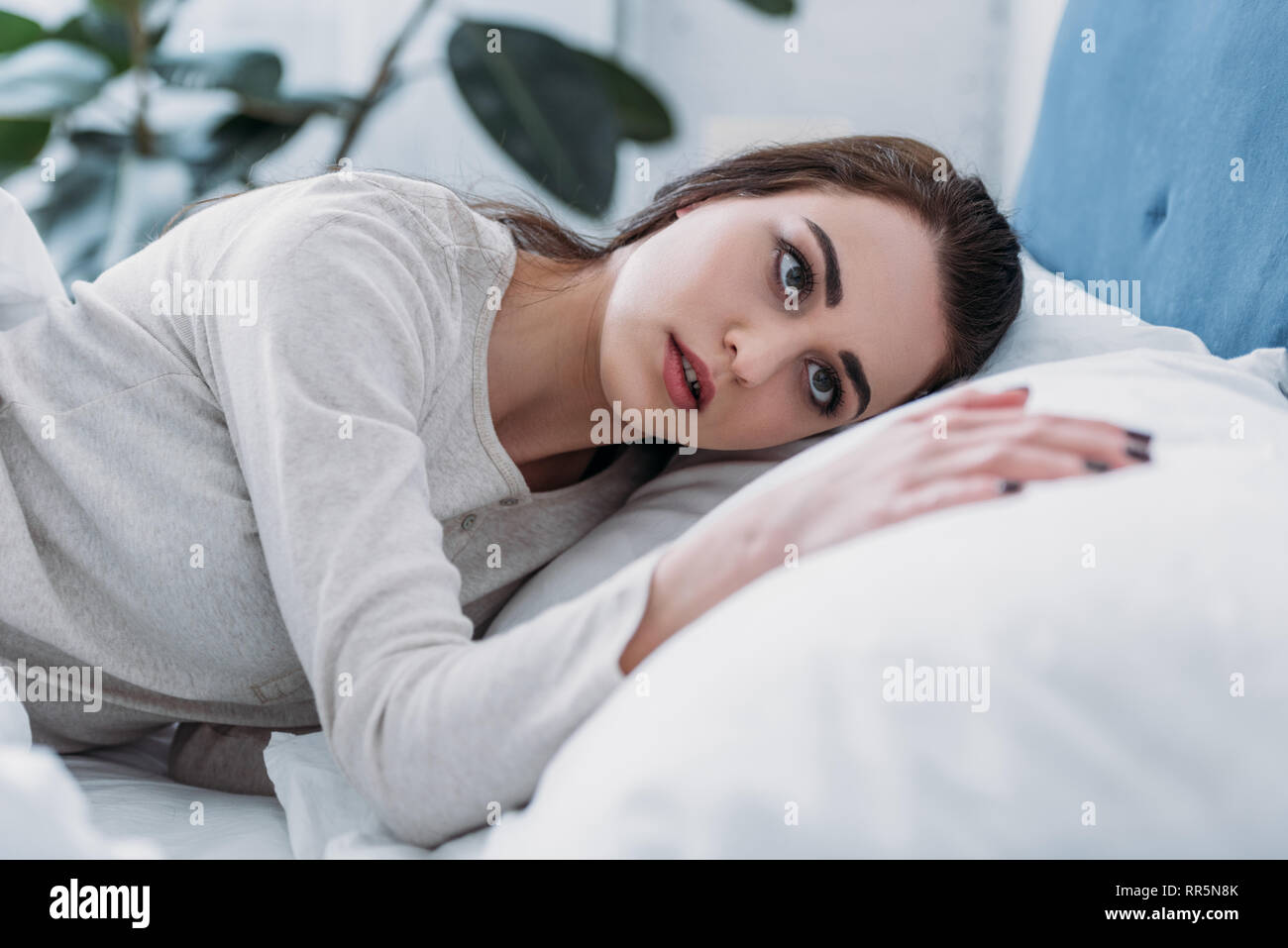 selective focus of beautiful sad woman in pajamas lying in bed at home ...