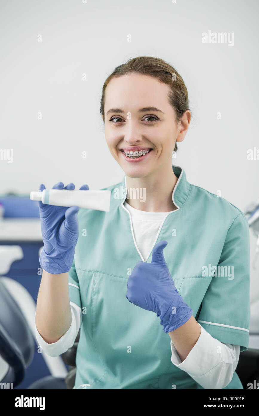 cheerful female dentist with braces on teeth holding toothpaste and ...