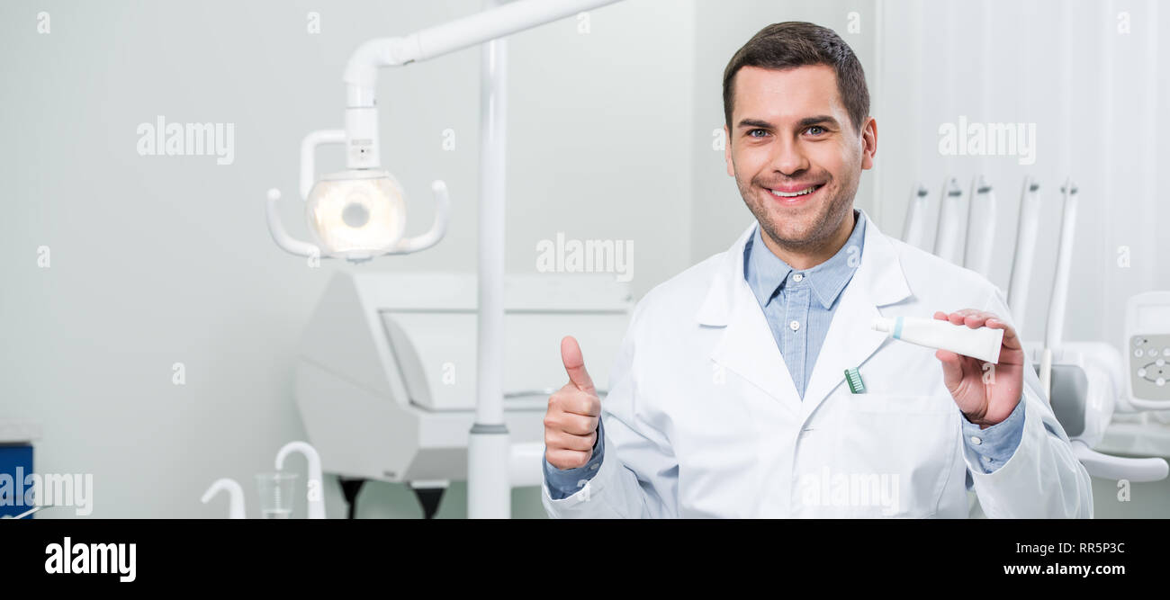 handsome dentist holding toothpaste and showing thumb up in dental ...