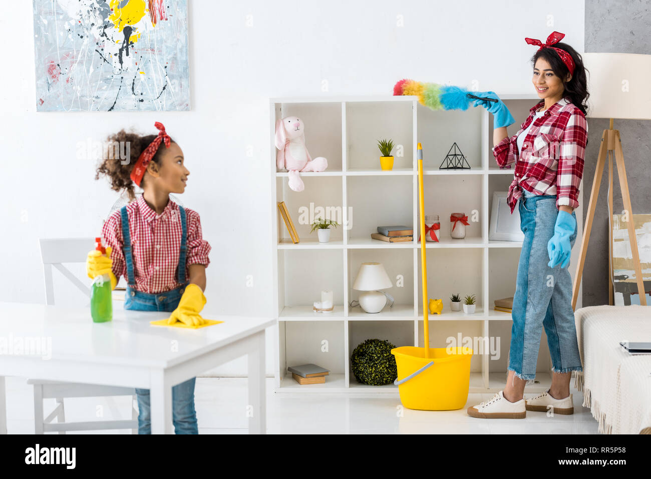 cute african american child cleaning table while mother dusting ...