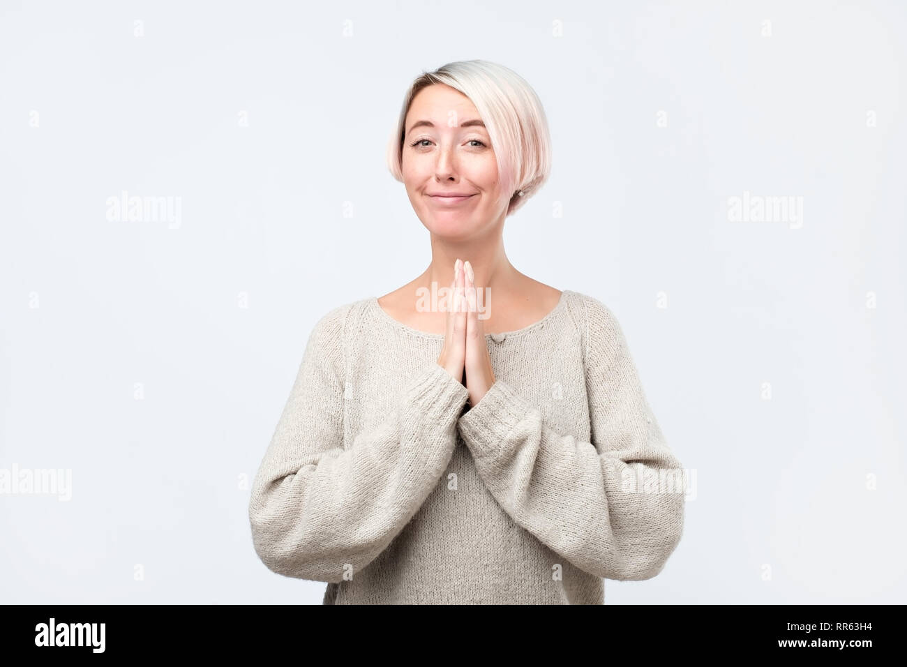 Woman with appealing look holding palms pressed together in front of ...