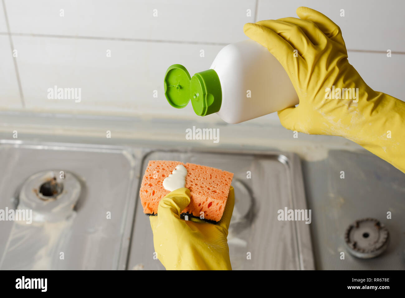 Two hands applying liquid soap from cleanser bottle to orange sponge ...