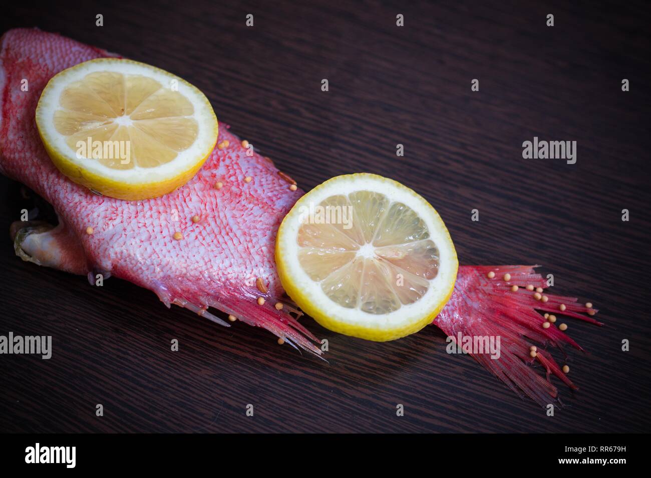 Two juicy lemon slices lie on fresh red fish. The fish is called sea ...