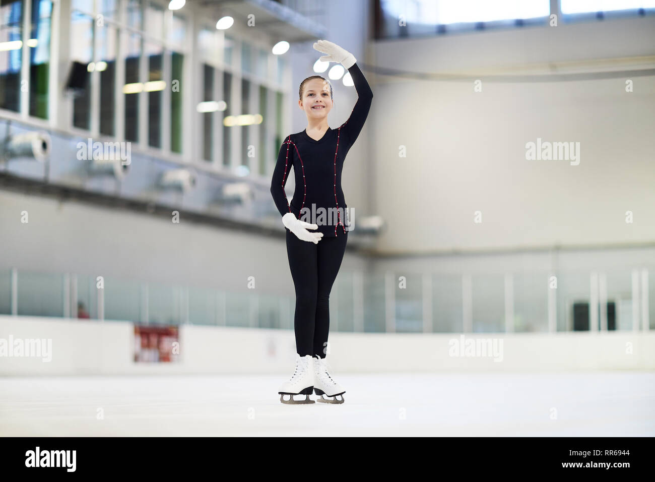 Full length portrait of smiling teenage girl figure skating on ice rink ...
