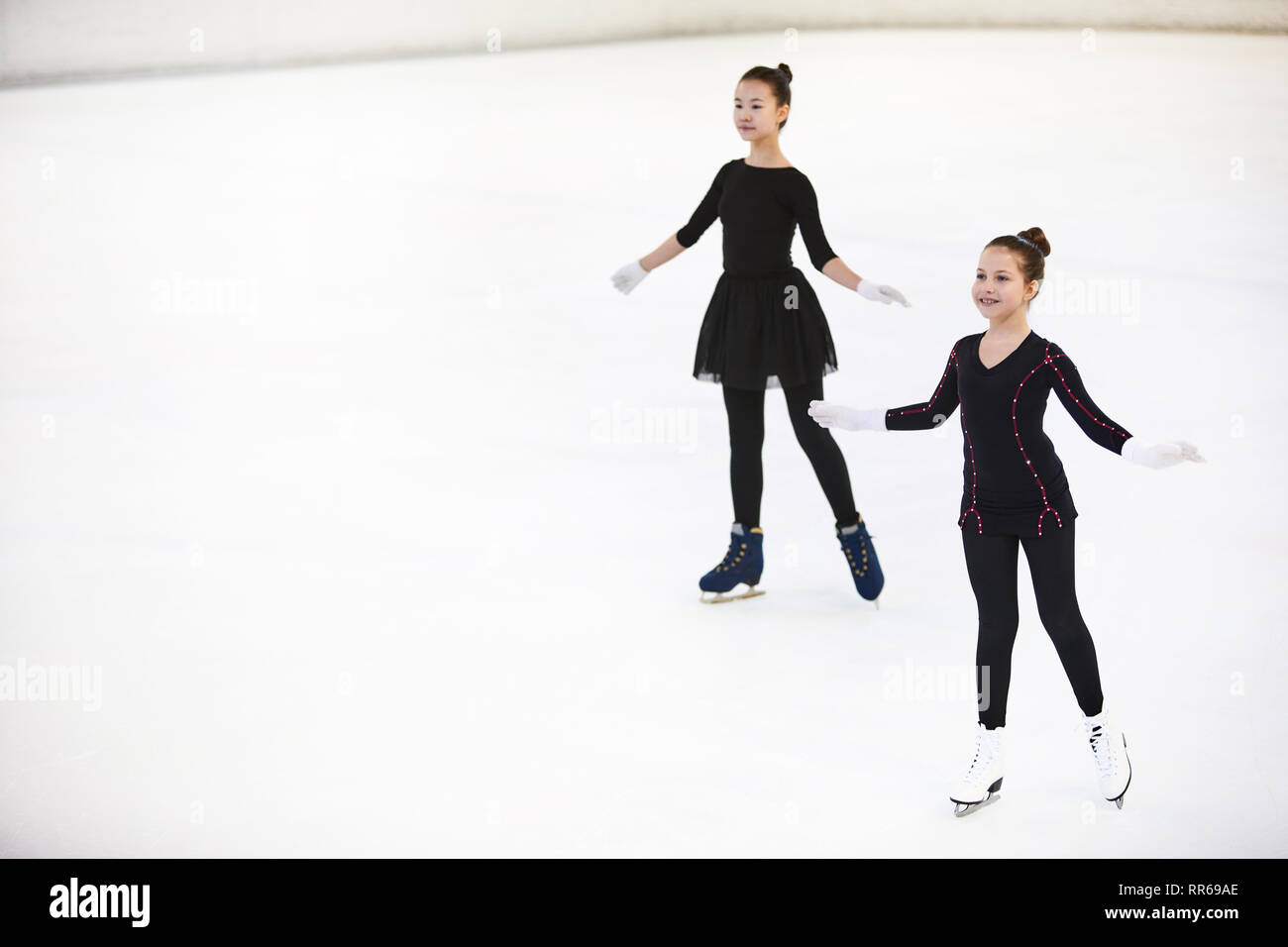 High angle portrait of two happy girls figure skating on ice rink ...