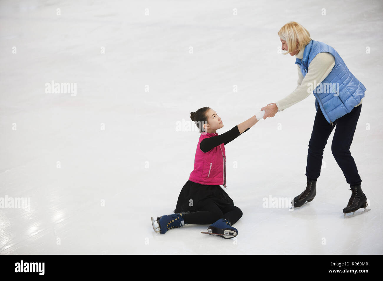 Full length portrait of mature female coach helping figure skater ...