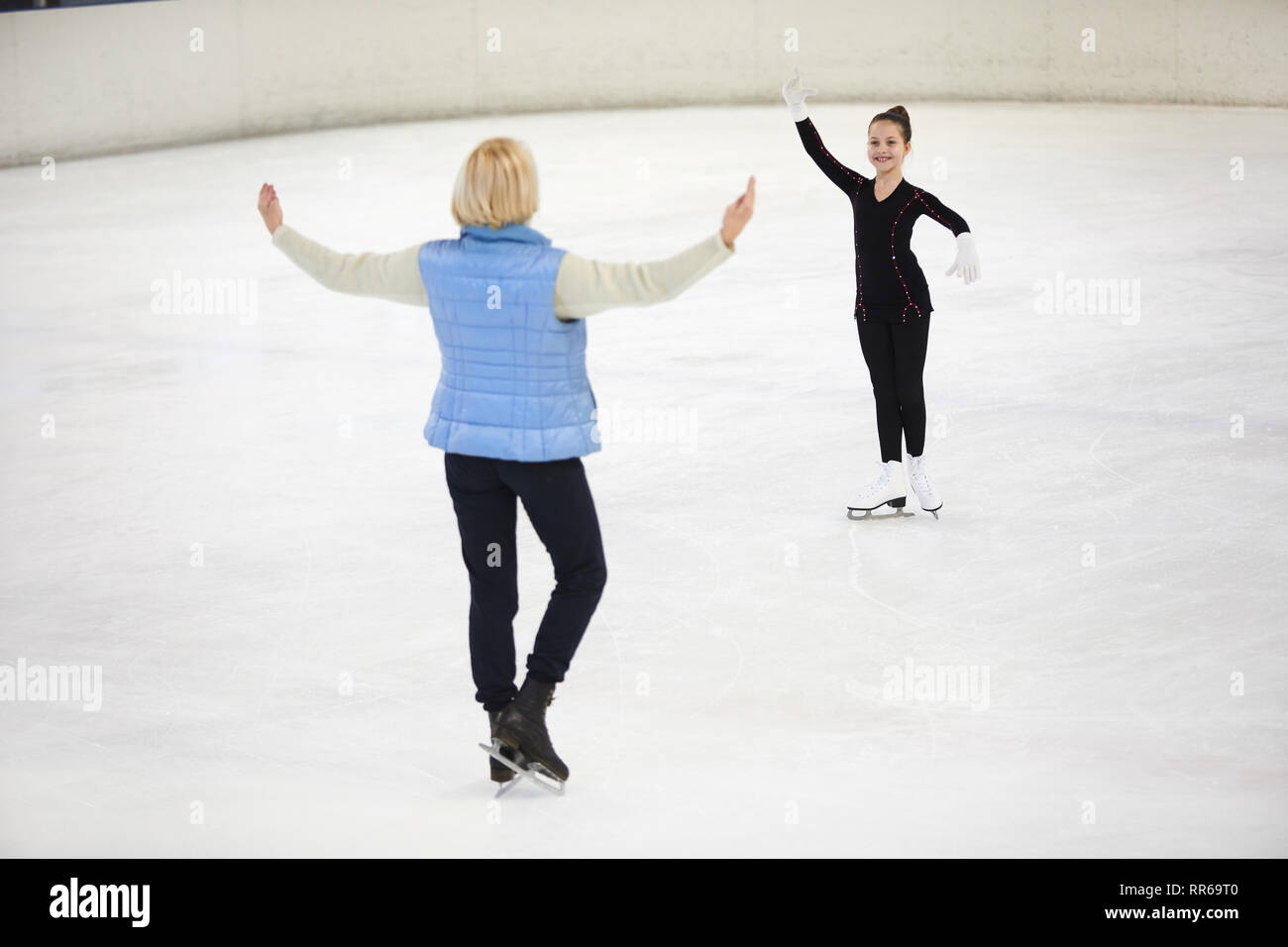 Full length portrait of happy girl figure skating on rink with female ...