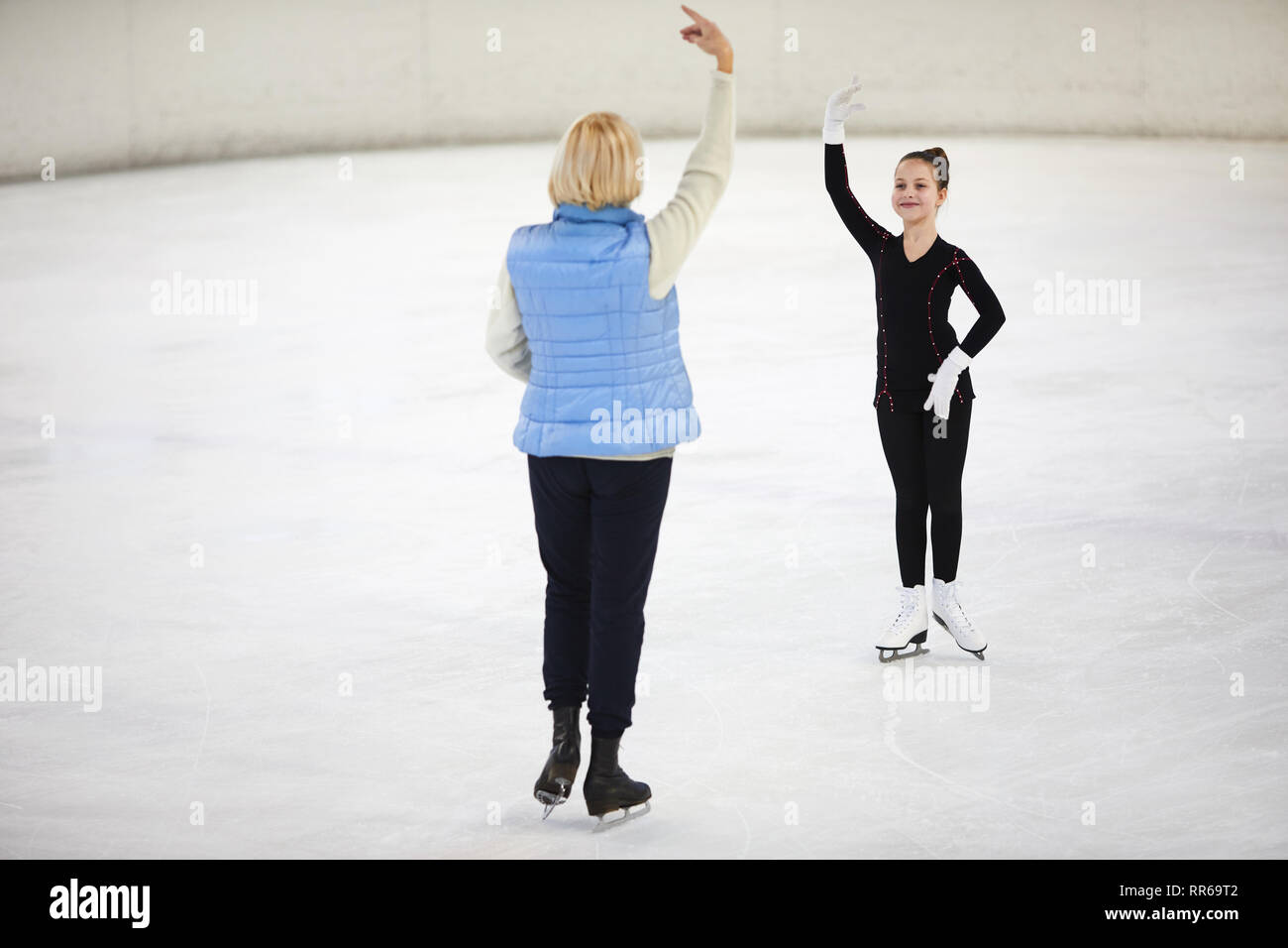 Full length portrait of smiling girl figure skating on rink with female ...